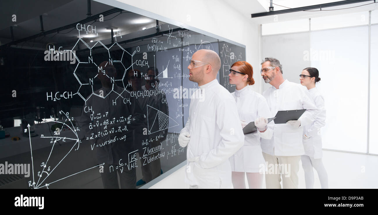side-view of four scientists in a chemistry lab analyzing formulas on a ...