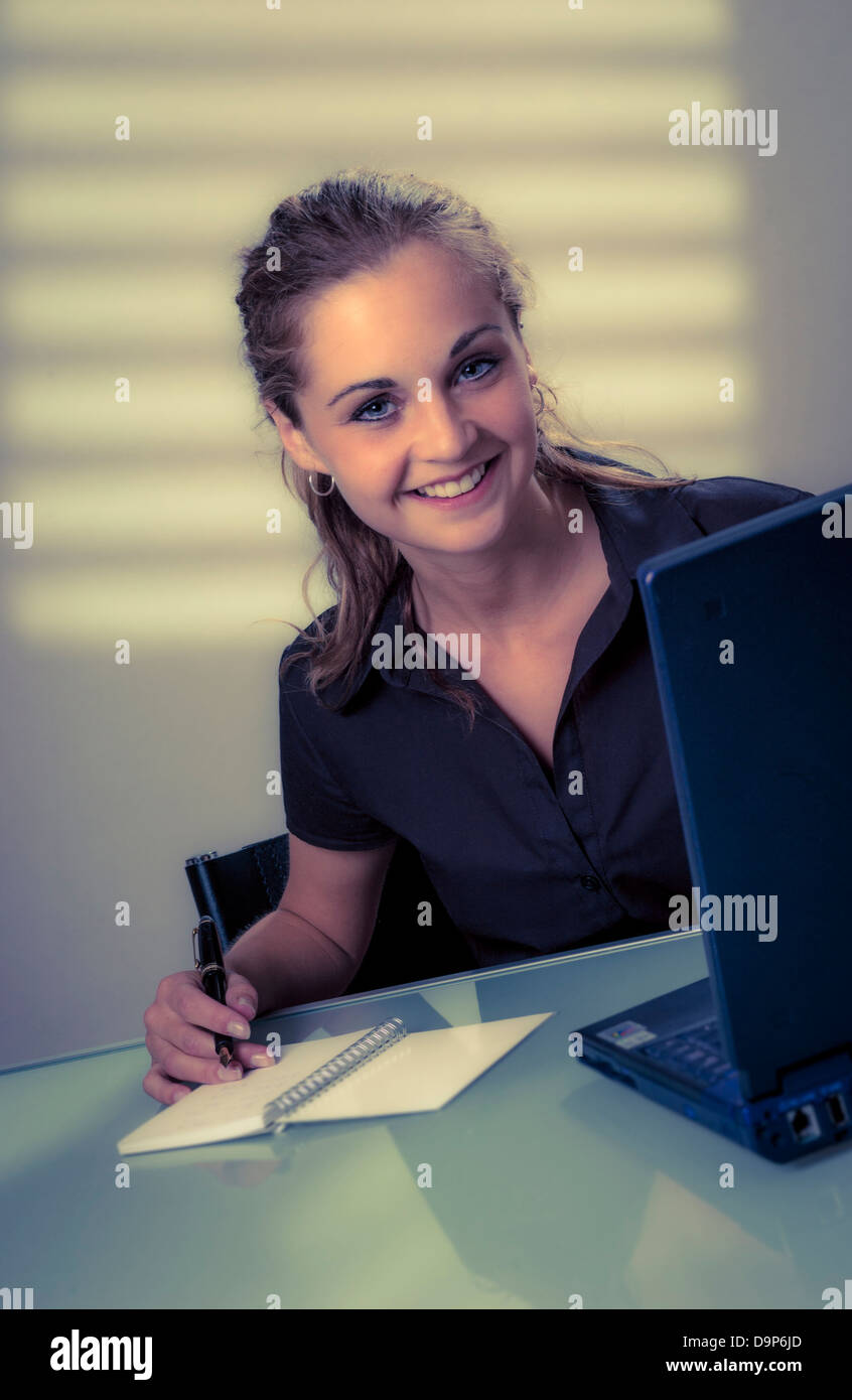 Young caucasian female sitting at desk with a laptop computer smiling ...