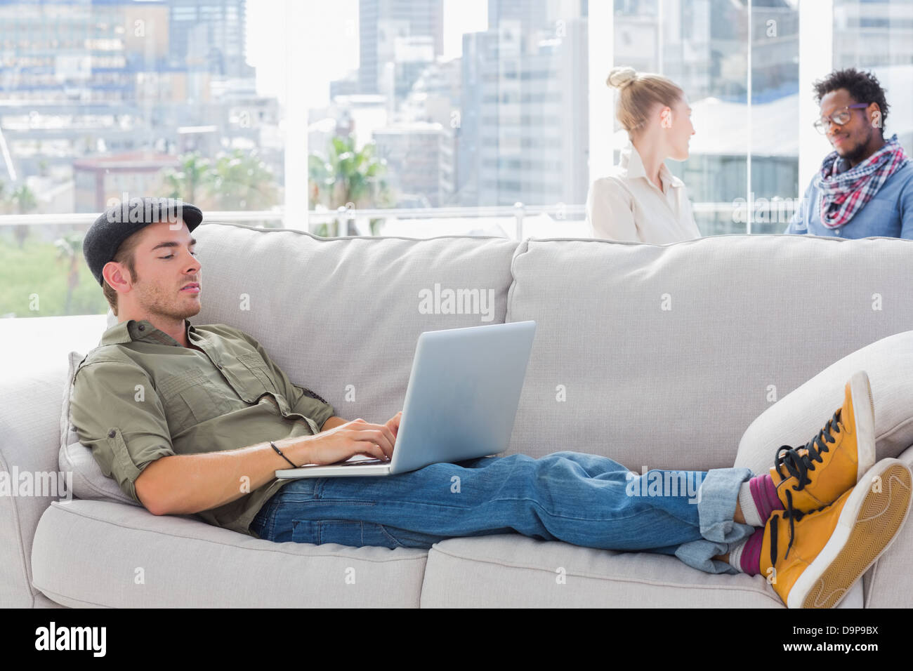 Worker using his laptop while laying on a couch Stock Photo - Alamy