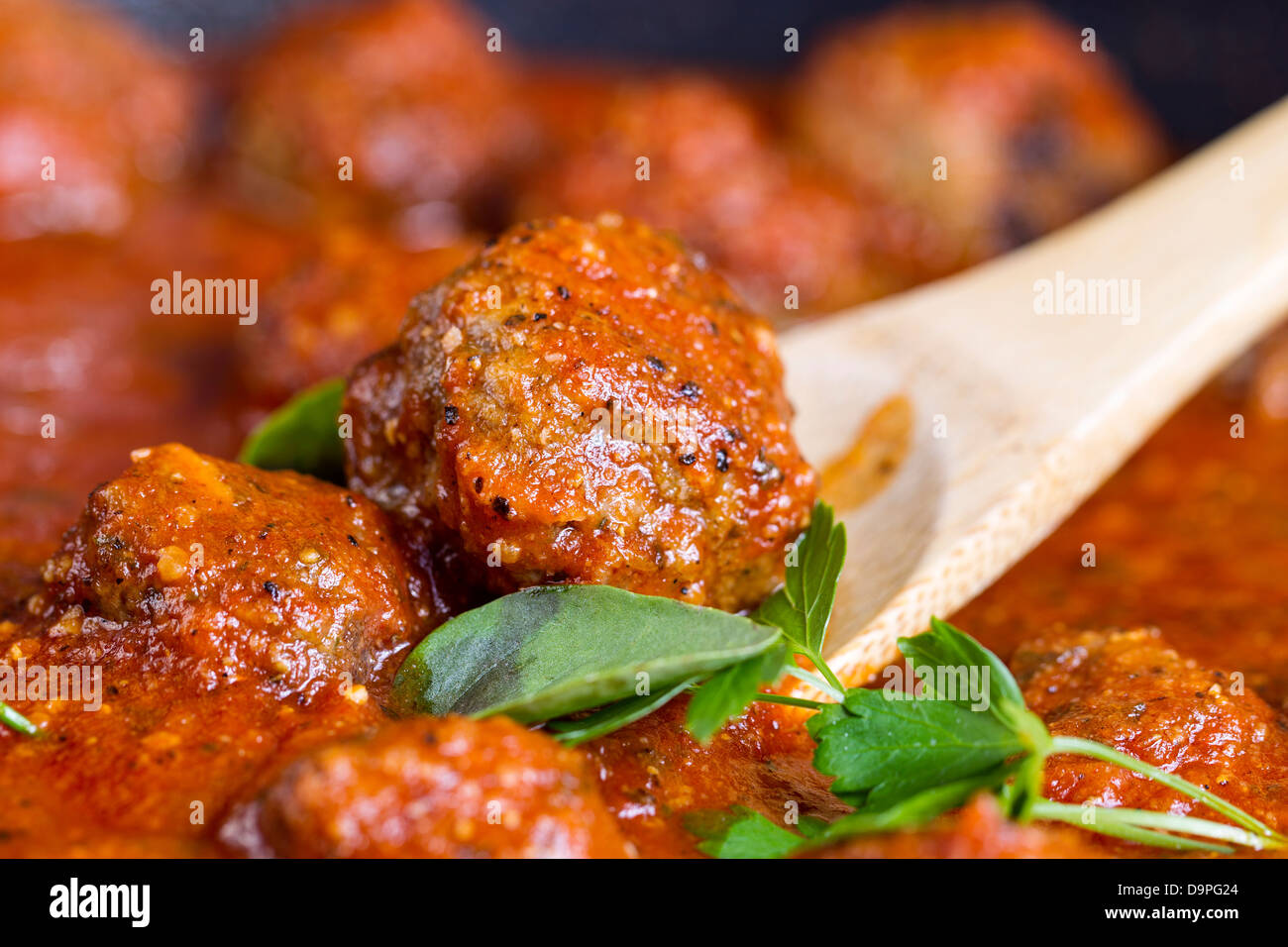 Horizontal photo of bread coated meatball in wooden spoon with basil ...