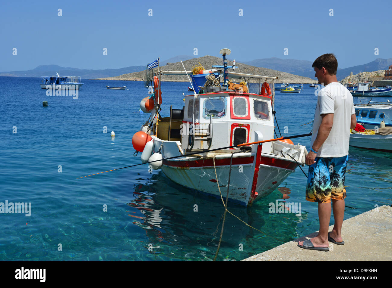 Young man fishing on waterfront, Port of Emporio, Halki (Chalki ...
