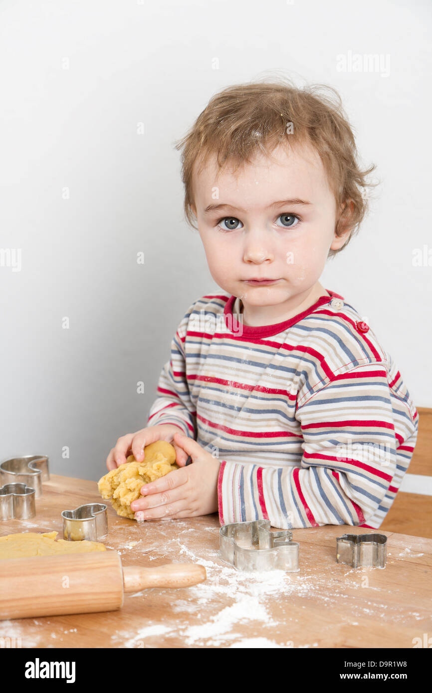 vertical image of 2 year old child making biscuit at wooden desk Stock ...