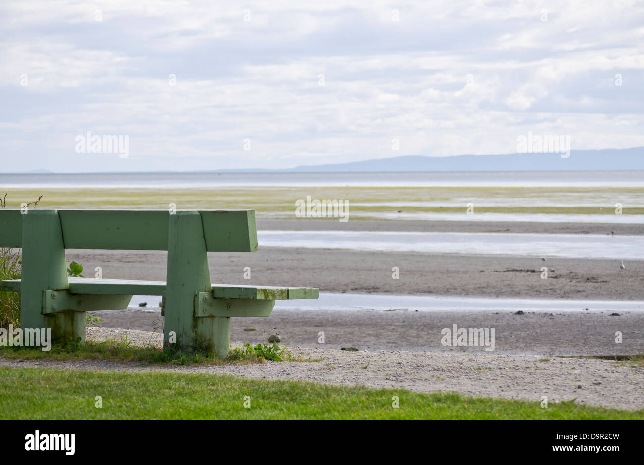 Empty seaside bench facing the ocean at low tide. At Crescent Beach, in ...