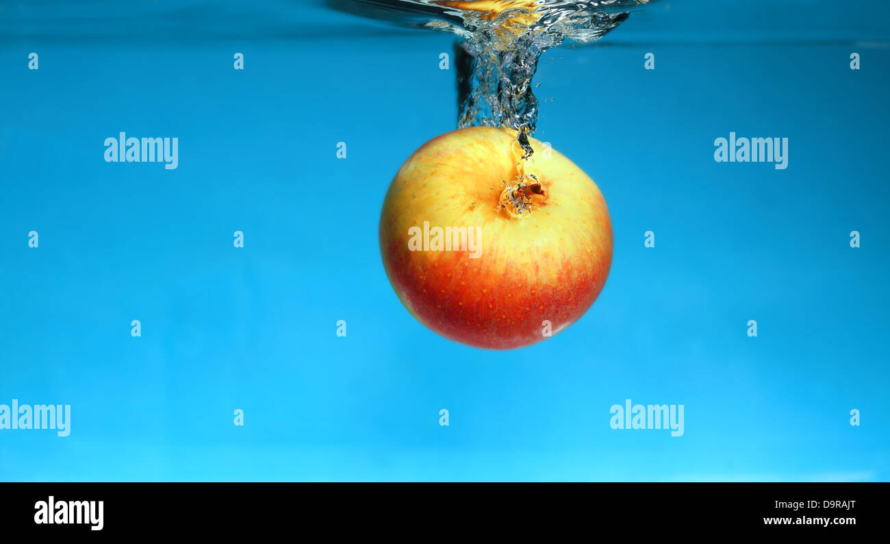 Yellow red apple in the water splash over blue background. Healthy food ...