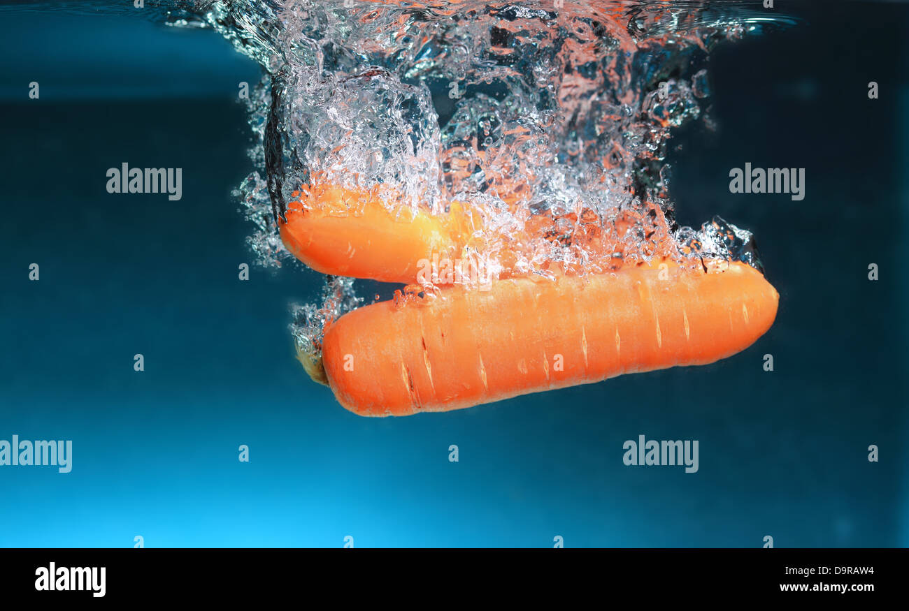 Carrot in the water splash over blue background. Healthy food and ...
