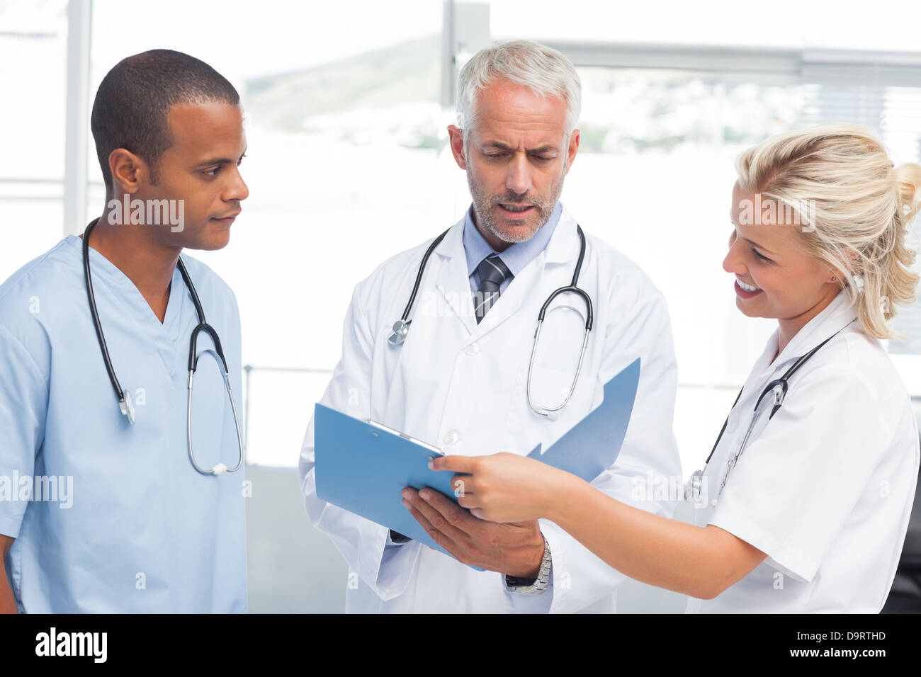 Three serious doctors examining a file Stock Photo - Alamy