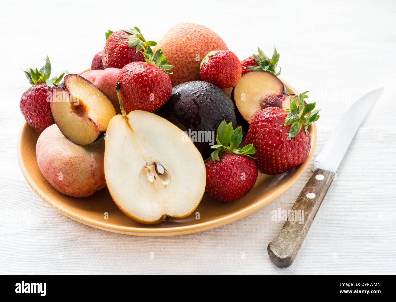 Fresh summer fruits in plate over light background with knife ...