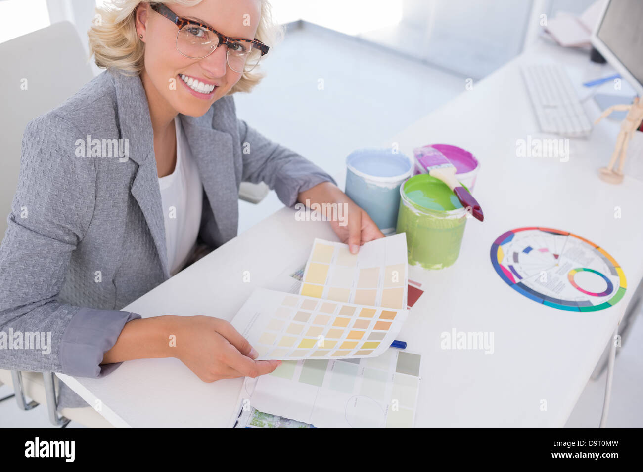 Blonde designer holding colour chart at her desk smiling at camera in ...