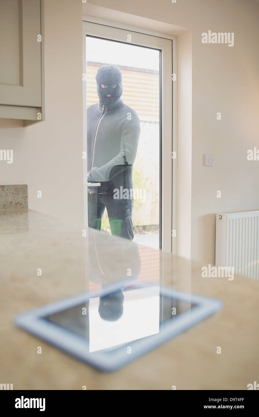 Burglar looking at tablet pc through kitchen door Stock Photo - Alamy