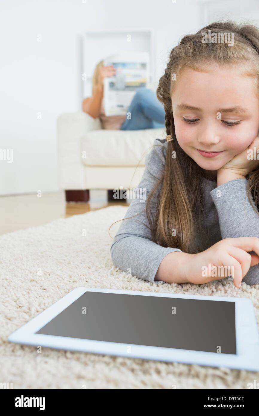 Girl using tablet with her mother reading the newspaper on the couch ...