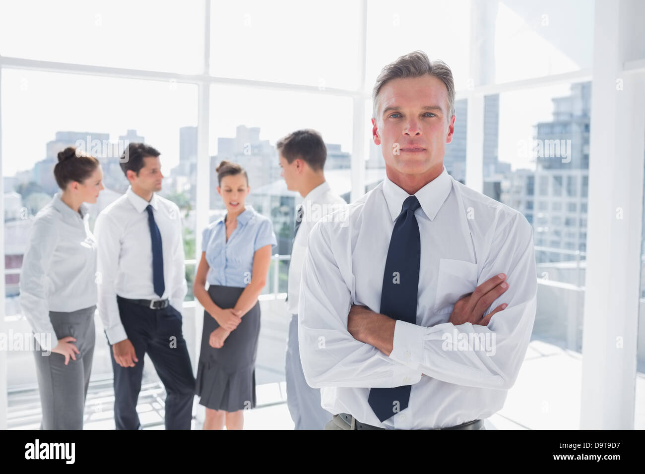 Serious boss with arms folded standing in a modern office Stock Photo ...