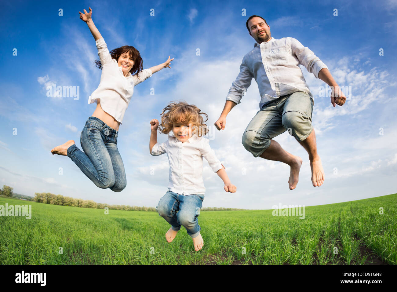 Happy active family jumping in green field against blue sky. Summer ...