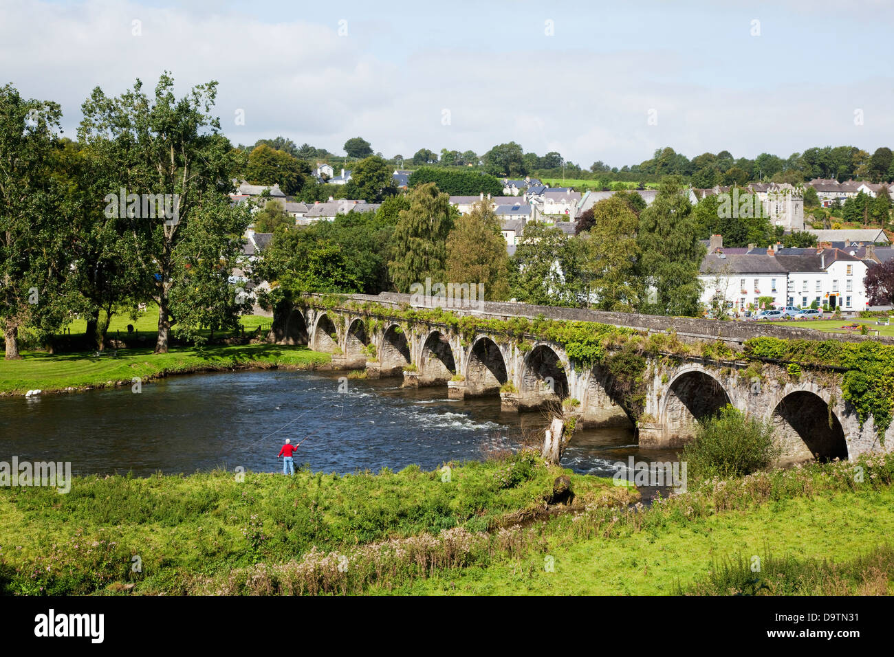 A bridge crossing the river nore with a man fishing at the water's edge ...