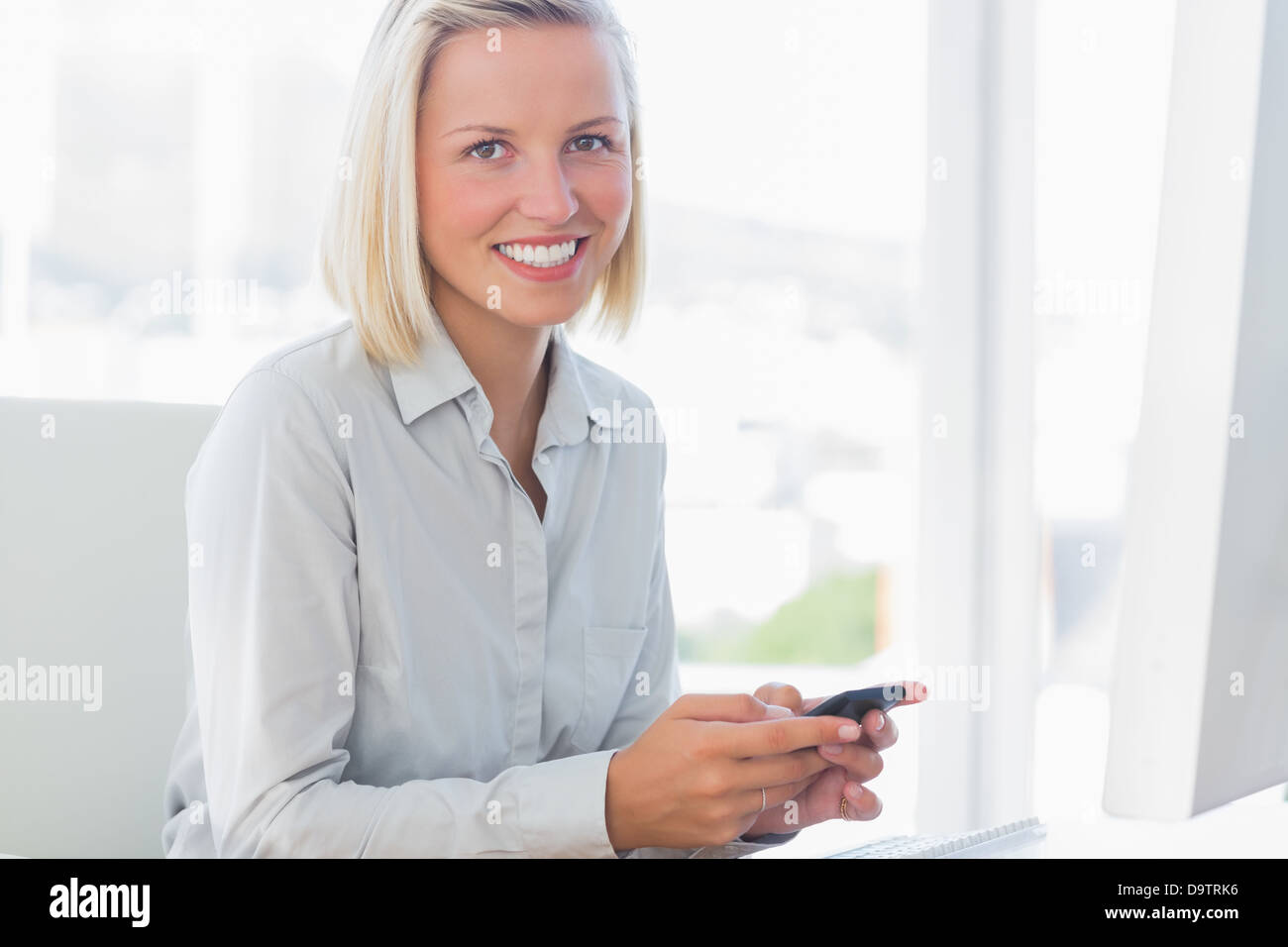 Blonde businesswoman texting and smiling at camera Stock Photo - Alamy