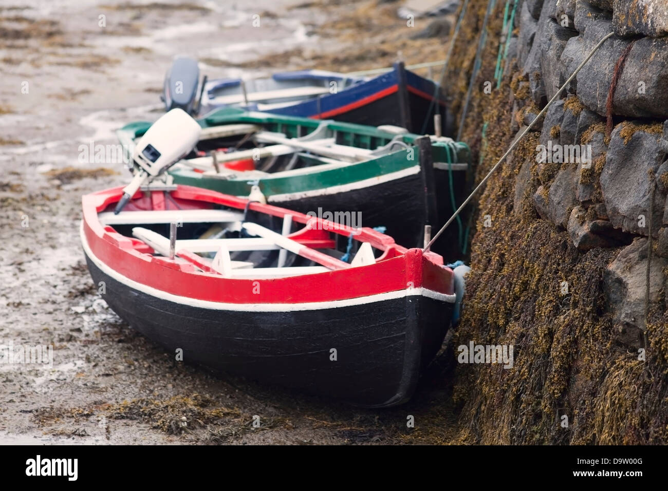 Three boats in a row on the shore against a stone wall;Roundstone ...