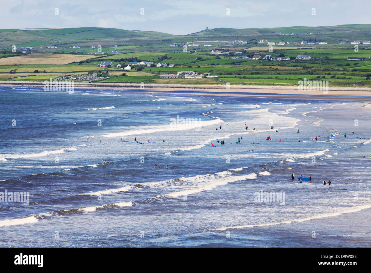 A busy beach with swimmers and surfers and houses scattered along the ...