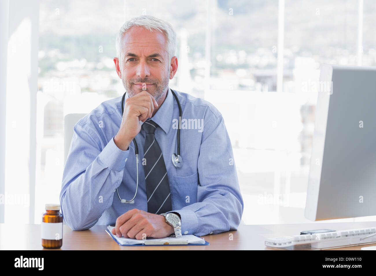 Cheerful doctor sitting behind his desk Stock Photo - Alamy