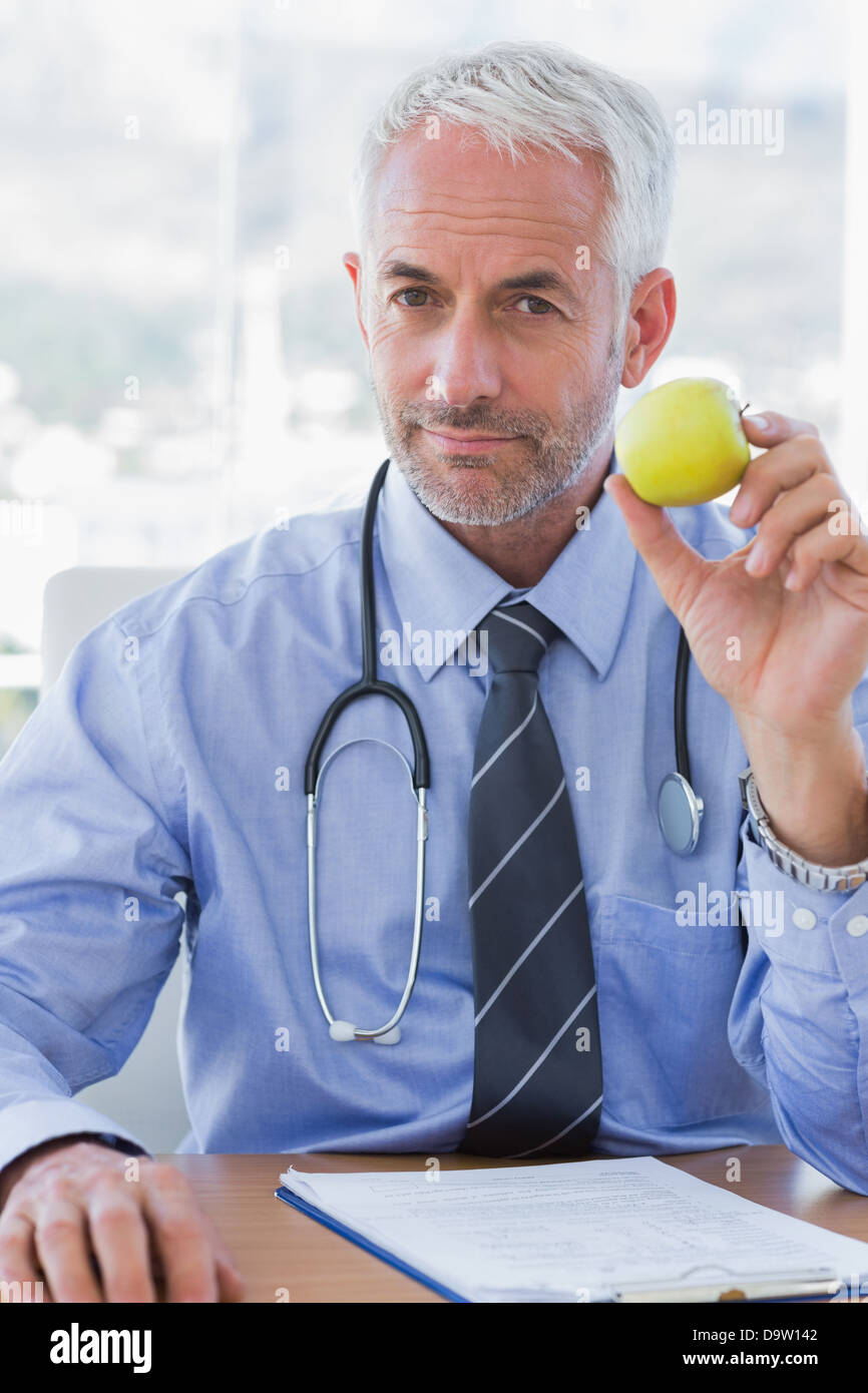 Doctor sitting behind his desk holding a green apple Stock Photo - Alamy