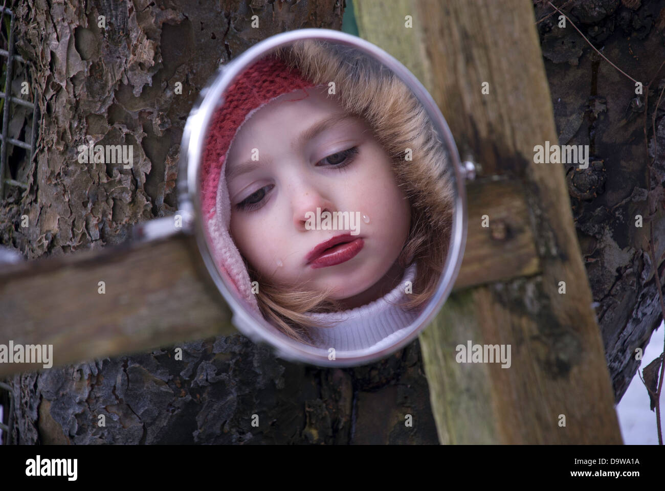 A young girl's face reflected in a mirror. She is crying and it is ...