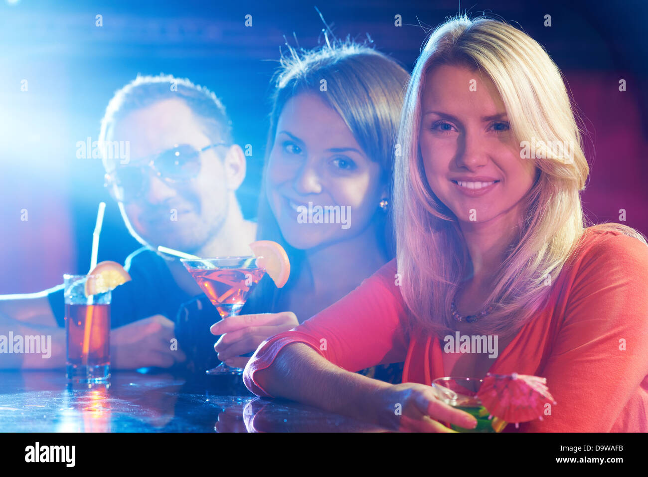 Three happy friends having party in bar, pretty blonde on foreground ...