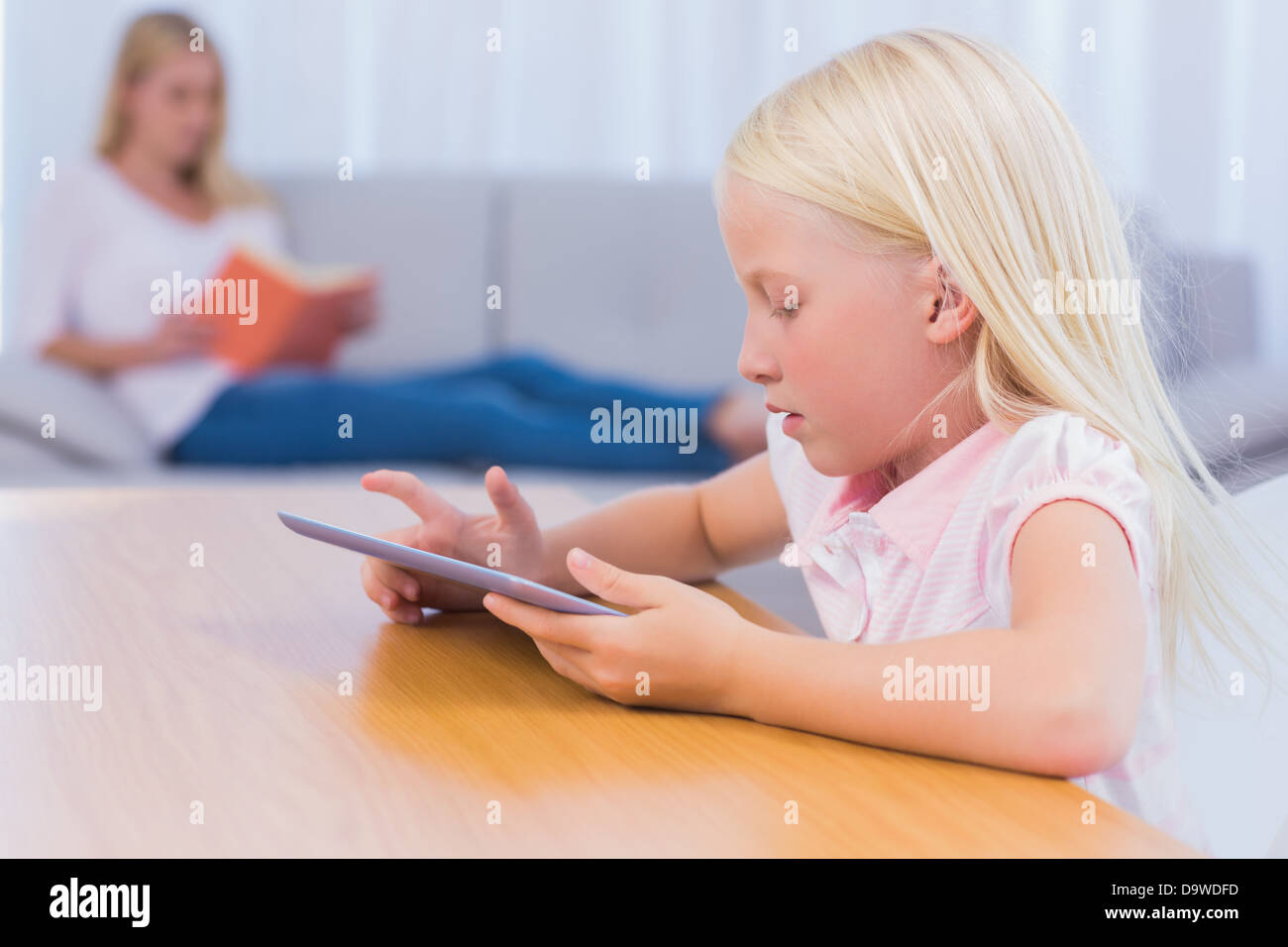 Little girl using tablet while her mother is reading on the couch Stock ...