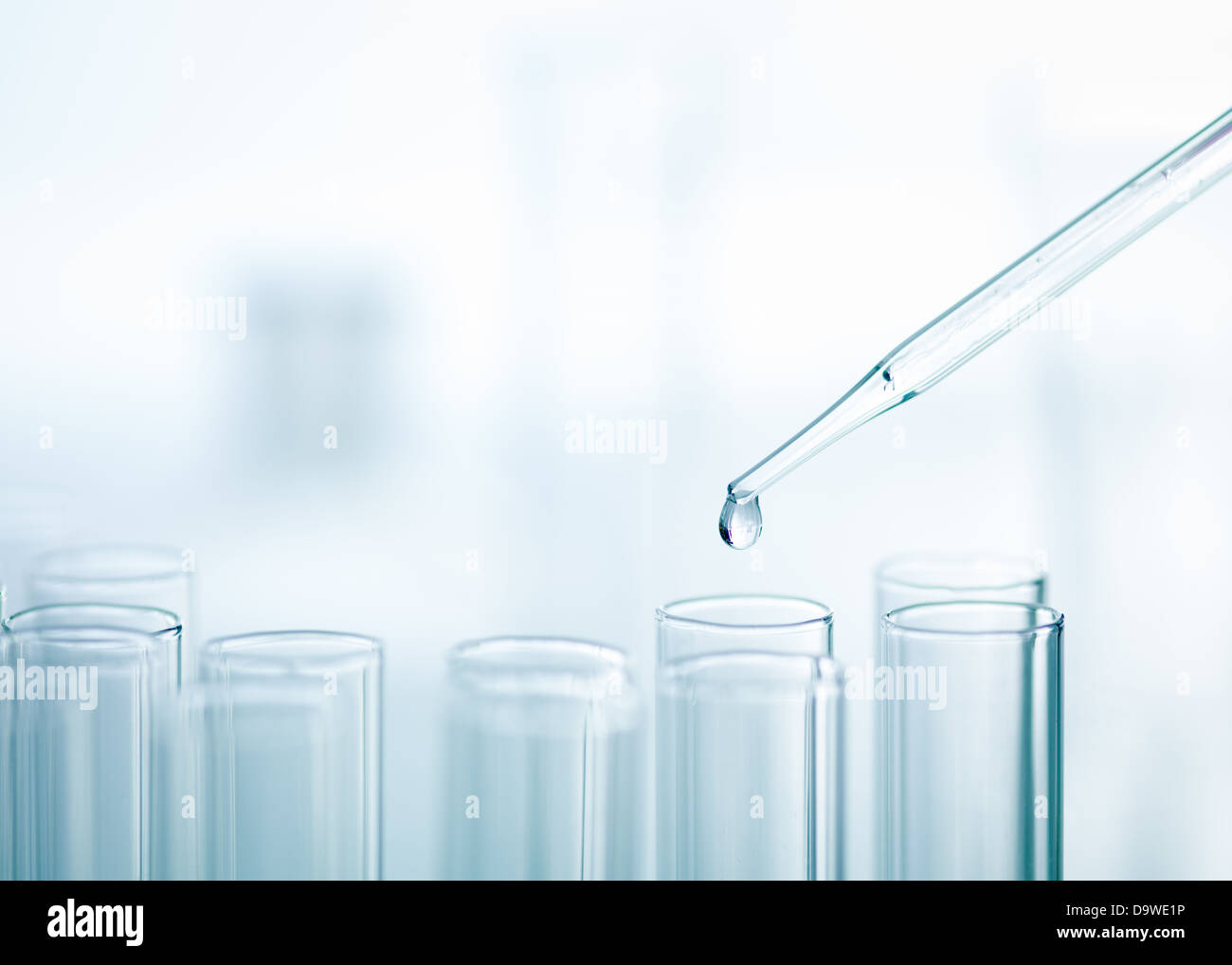 A close-up of a laboratory glass pipette with emerging drop of ...