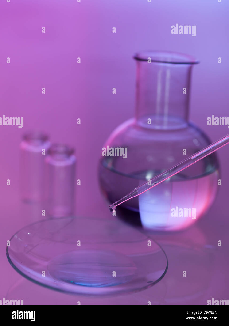 pipette dropping a transparent liquid in a dish with two empty beakers ...