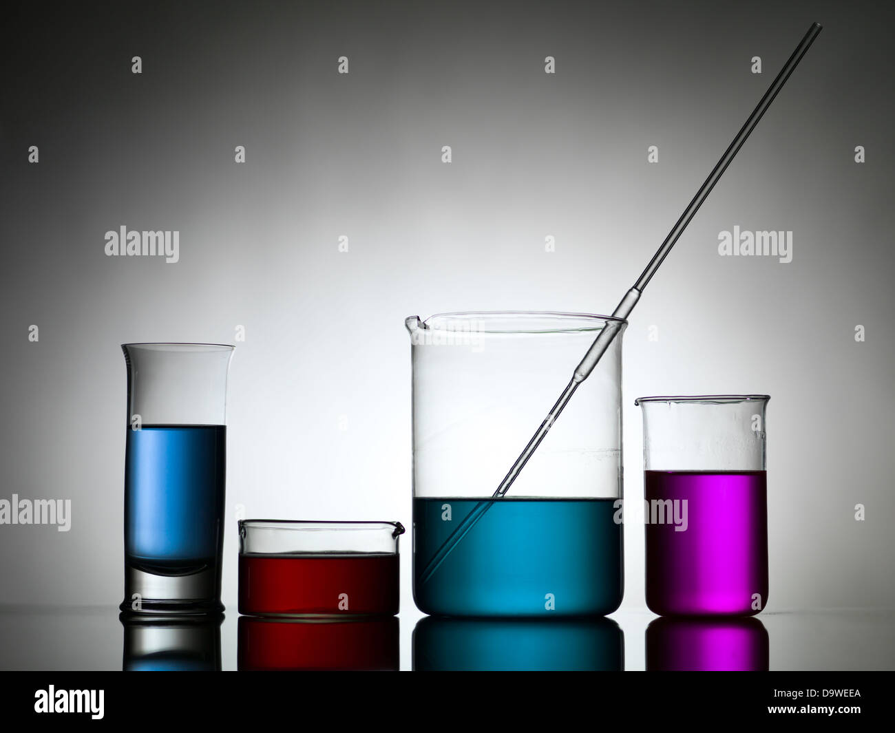 different sizes beakers filled with colored liquid whith a dropper in ...