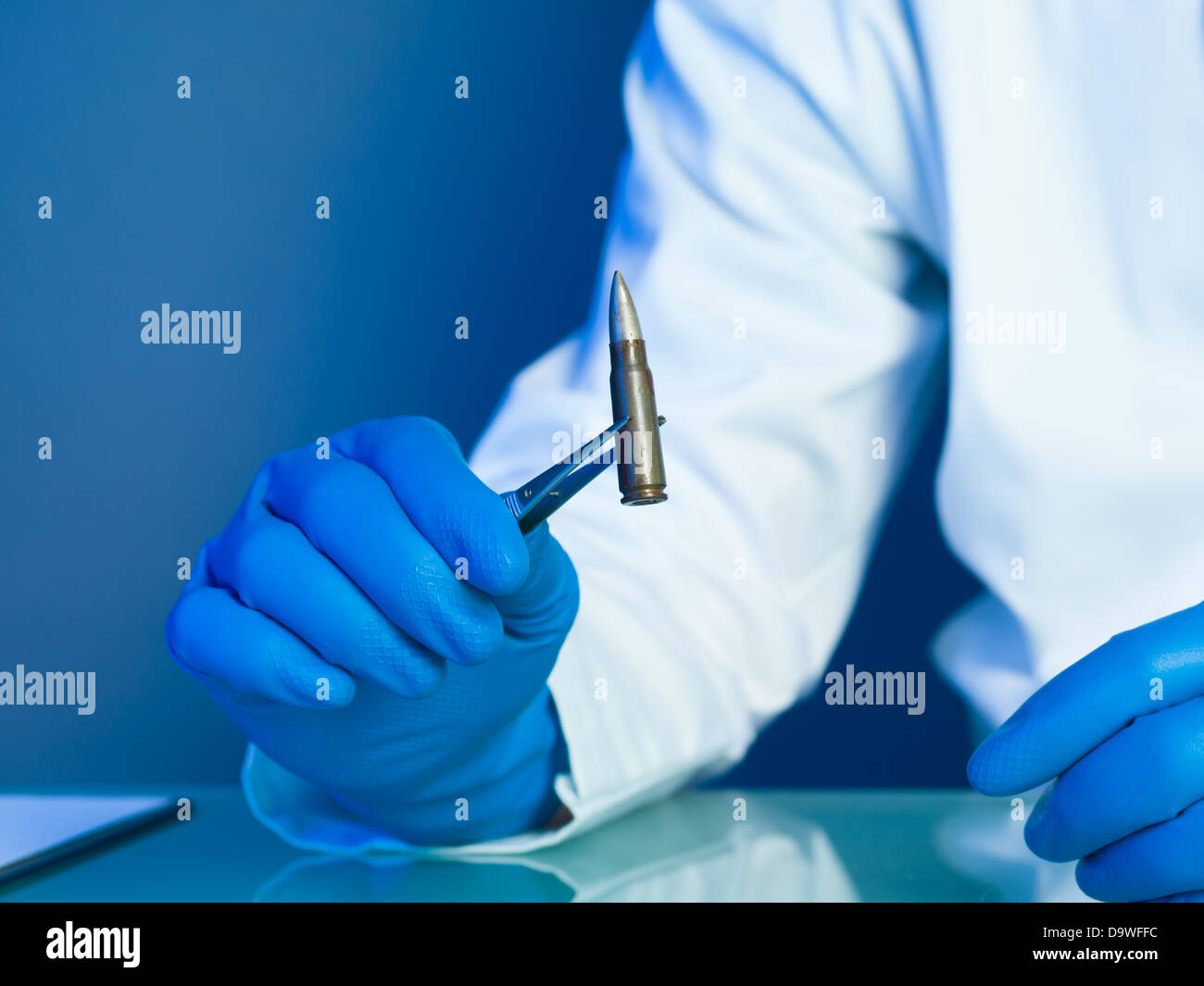 person in a white lab coat and blue rubber gloves, holding a bullet ...