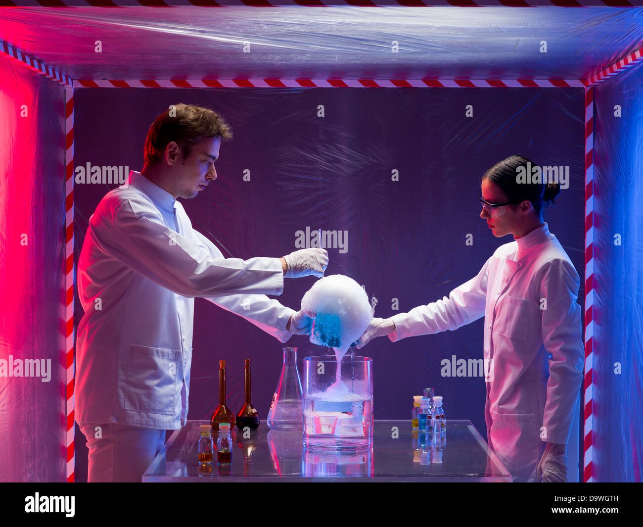two scientists, a man and a woman, mixing chemicals in a containment ...