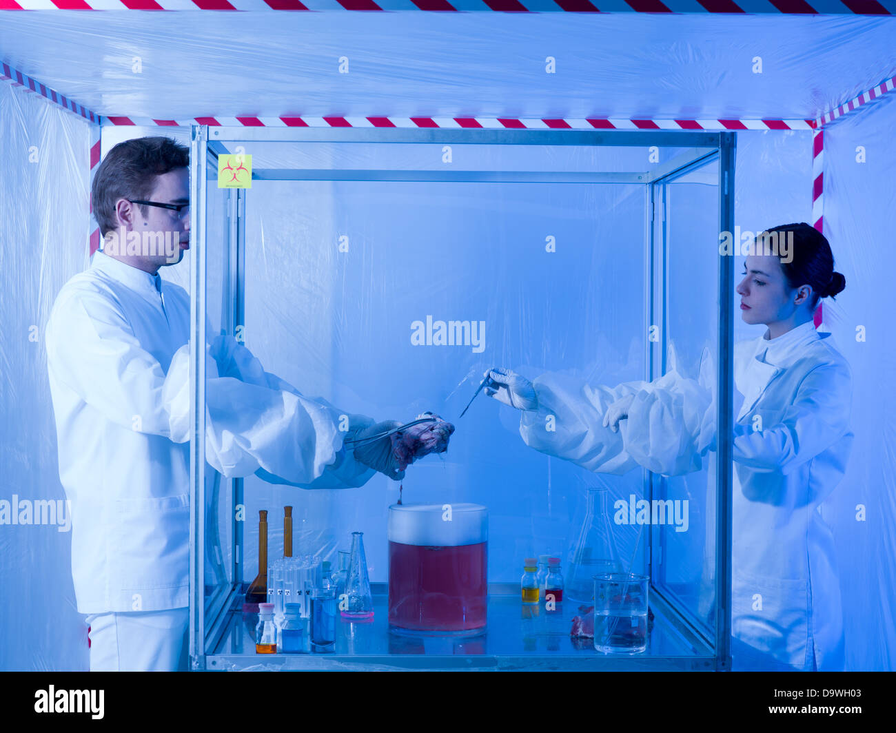 two scientists in a containment tent, a man and a woman, experimenting ...