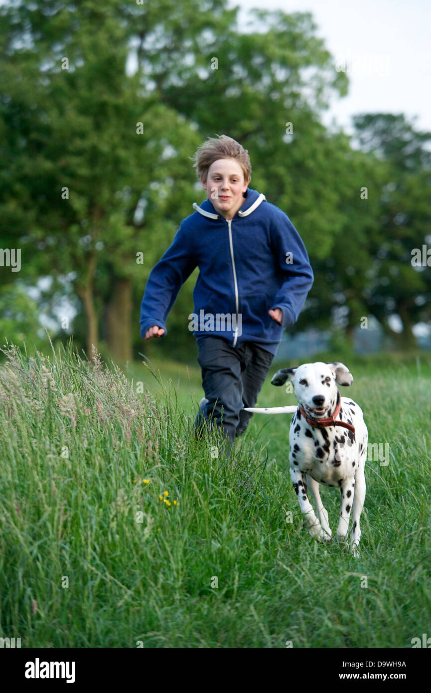 Young boy chases his pet Dalmatian dog through fields of long grass ...