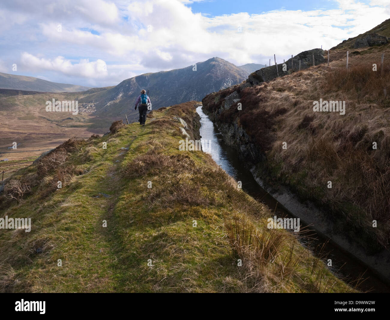 Walker follow leat around lower slopes of Y Braich in Snowdonia's ...