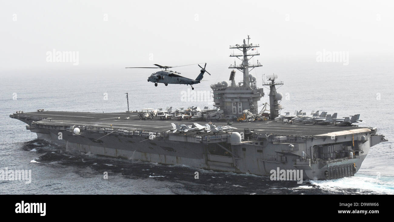 A US Navy MH-60S Sea Hawk helicopter flies by the aircraft carrier USS ...