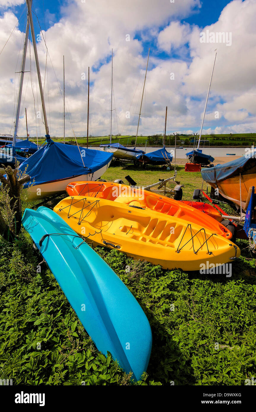 Three brightly coloured ocean kayaks, laid on a grassy bank in Alnmouth ...