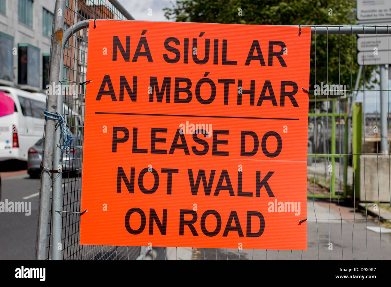 Road sign 'Please do not walk on road' attached to a fence of a ...