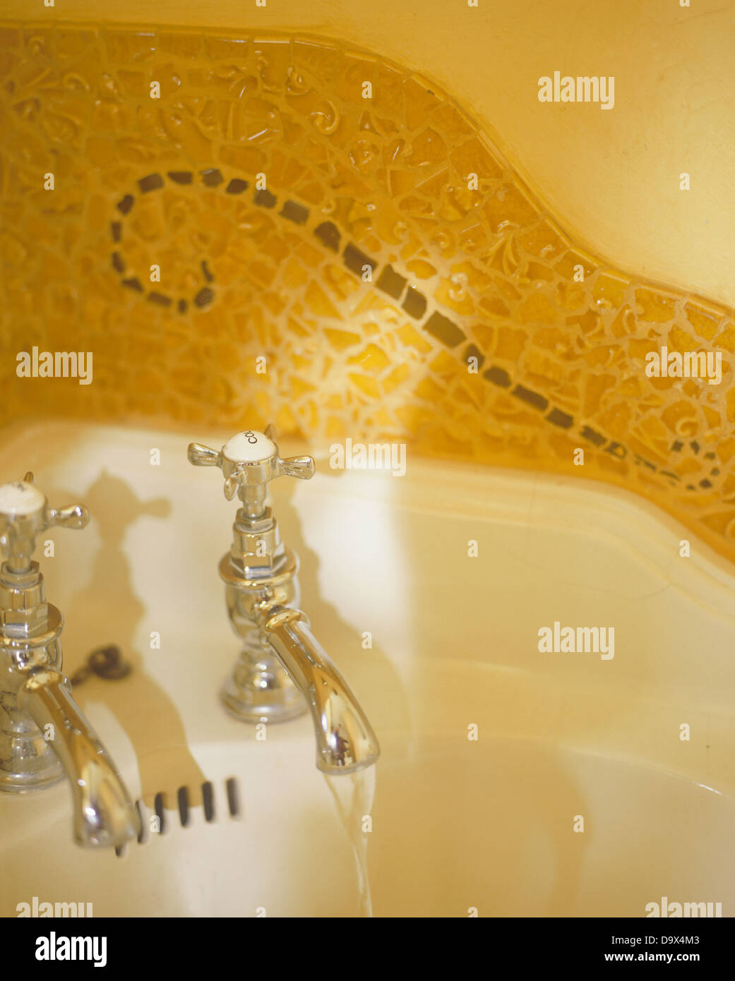 Chrome taps running water into basin below mosaic tiled splash-back ...