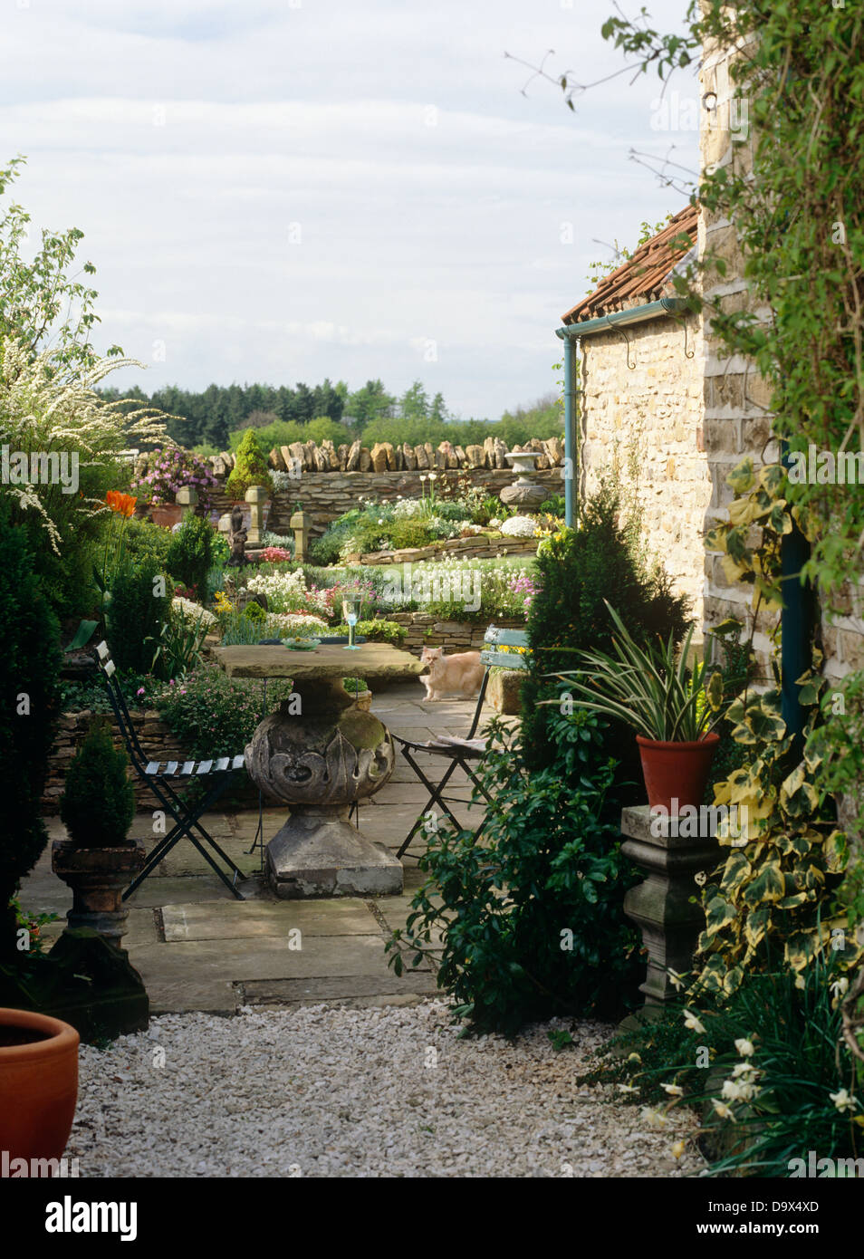 Stone table and slatted wooden chairs on stone paved terrace in garden ...