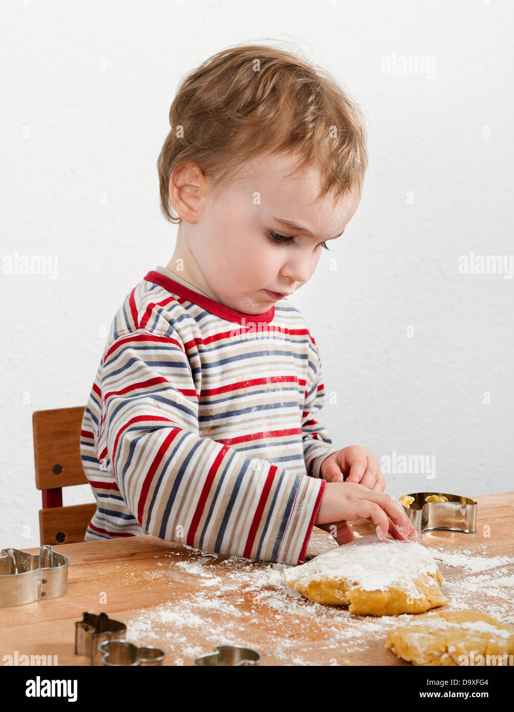 vertical image of 2 year old child making biscuit at wooden desk Stock ...