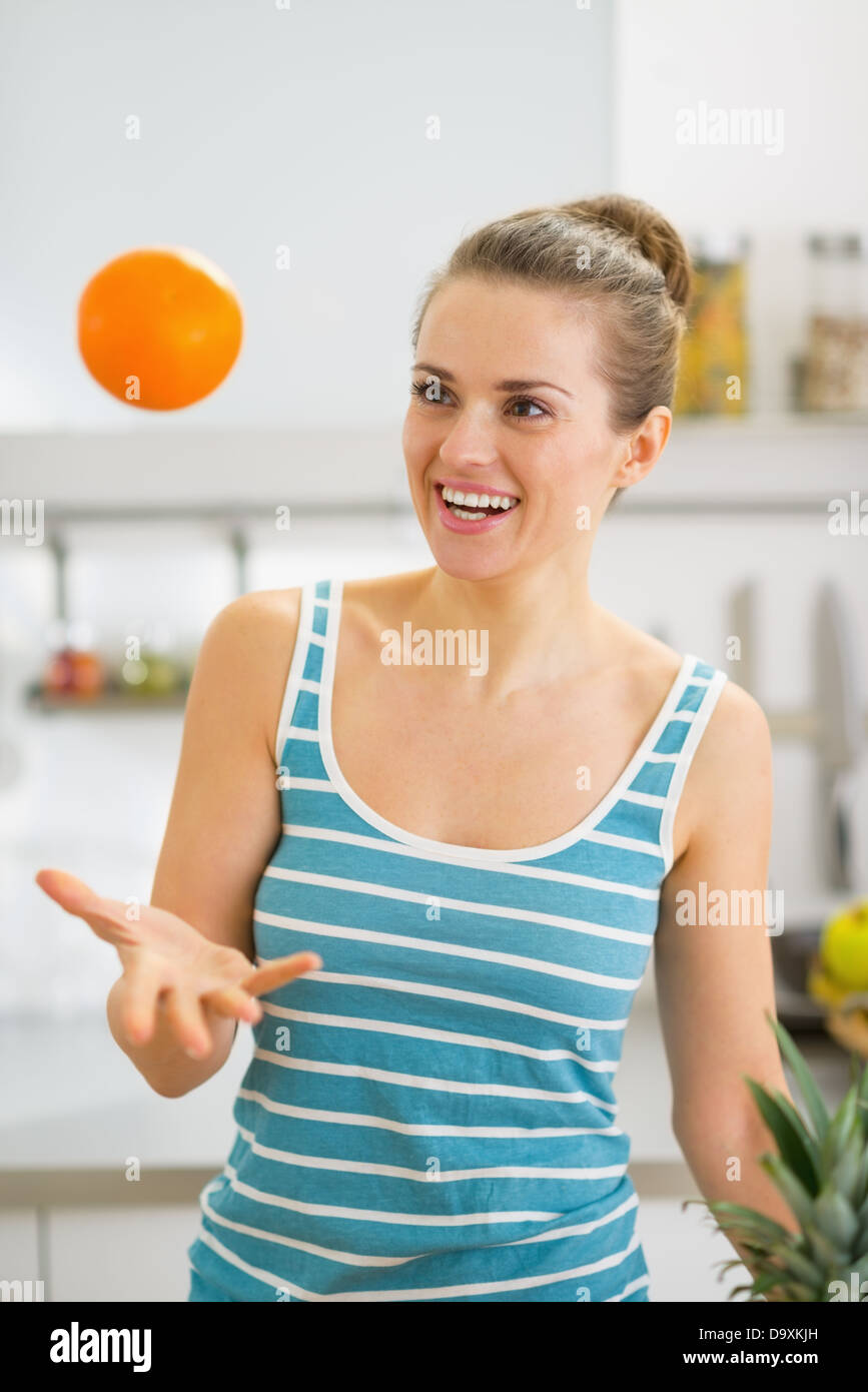 Happy young woman throwing orange in kitchen Stock Photo - Alamy