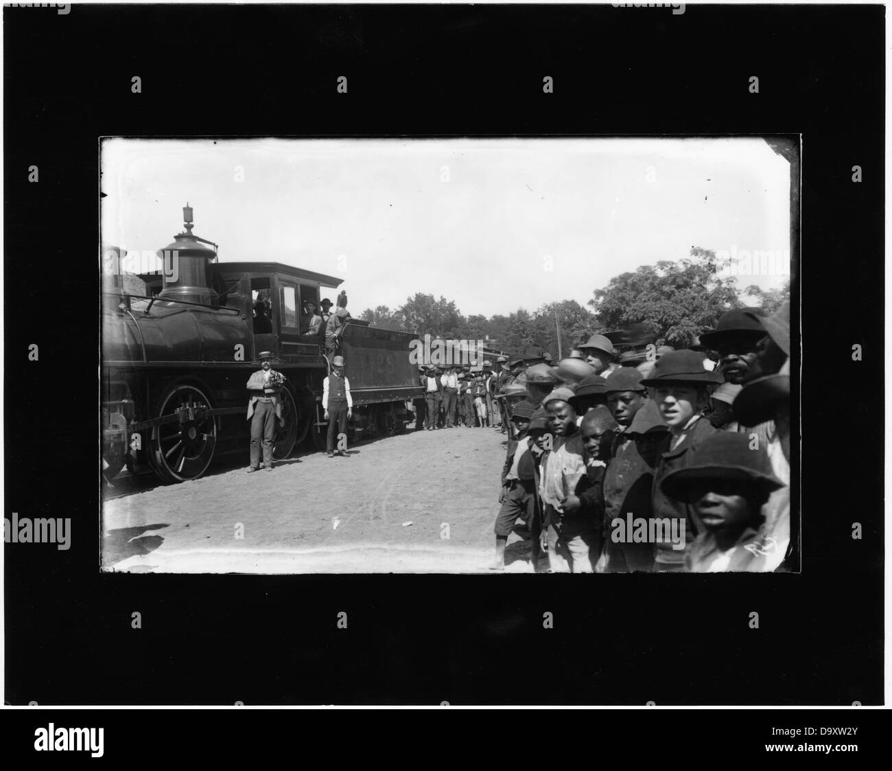 A photo of a train with people standing nearby. The image depicts a ...
