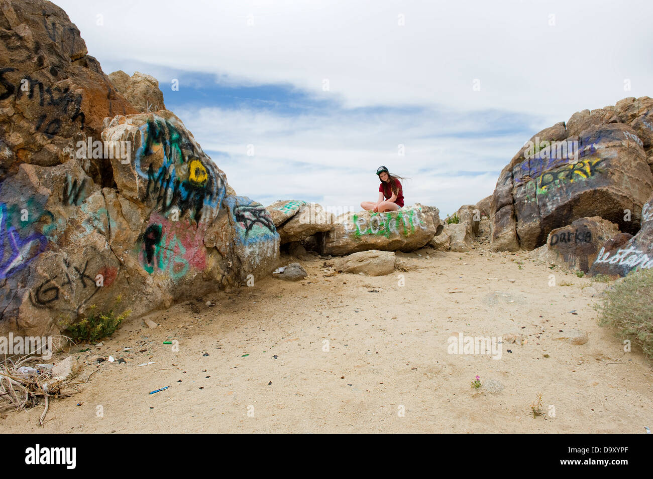 Teenage girl in 'OBAY' cap sitting on graffiti covered rocks in the ...