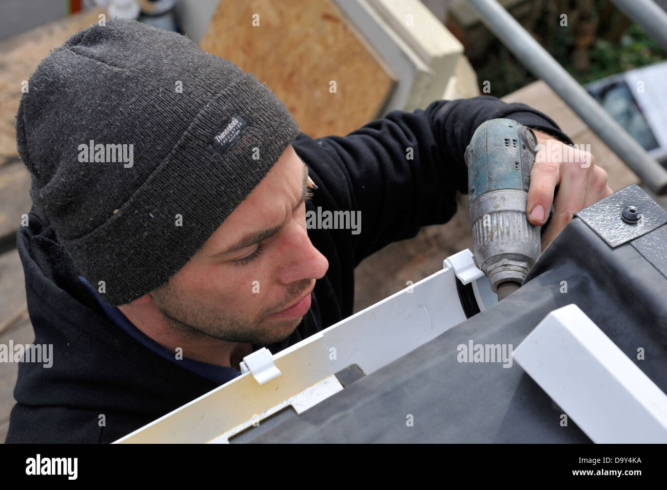 Builder installing a rainwater gutter on roof with cordless drill ...