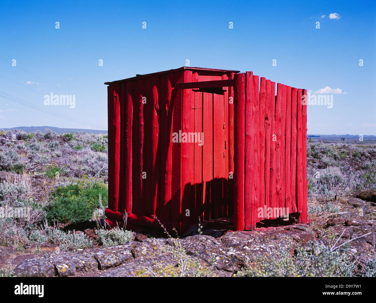 USA, Idaho, Bright red vertical log outhouse on lava plain at Shoshone ...