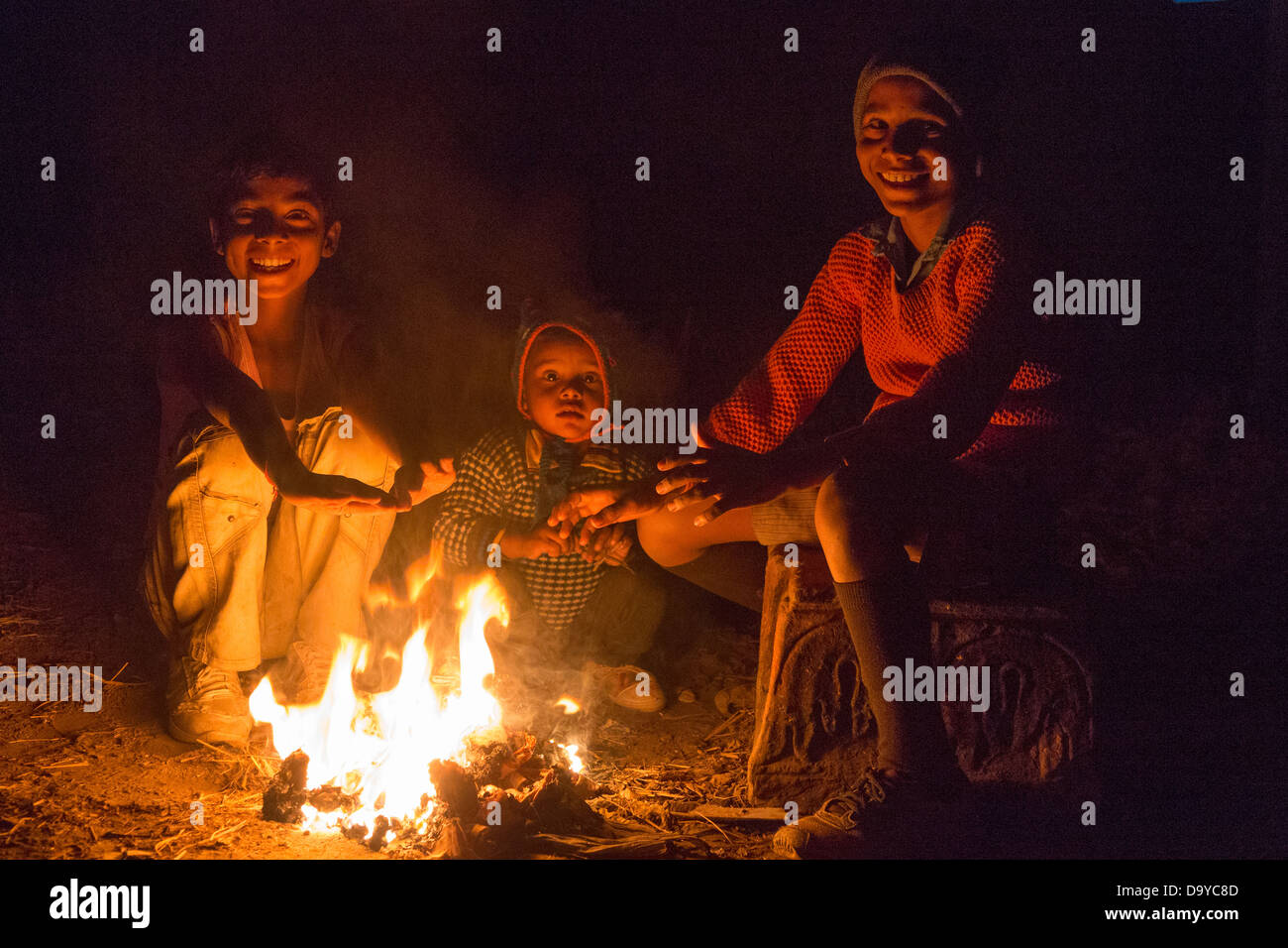 India, Uttar Pradesh, Agra, three children sitting around fire at night ...
