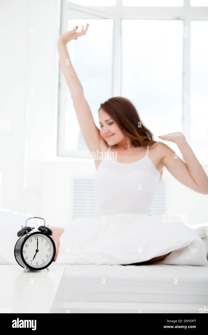 Tired sleepy woman waking up and giving a stretch while sitting in bed ...