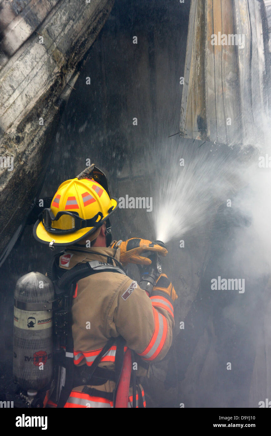 A firefighter spraying water on a structure fire hotspot Stock Photo ...