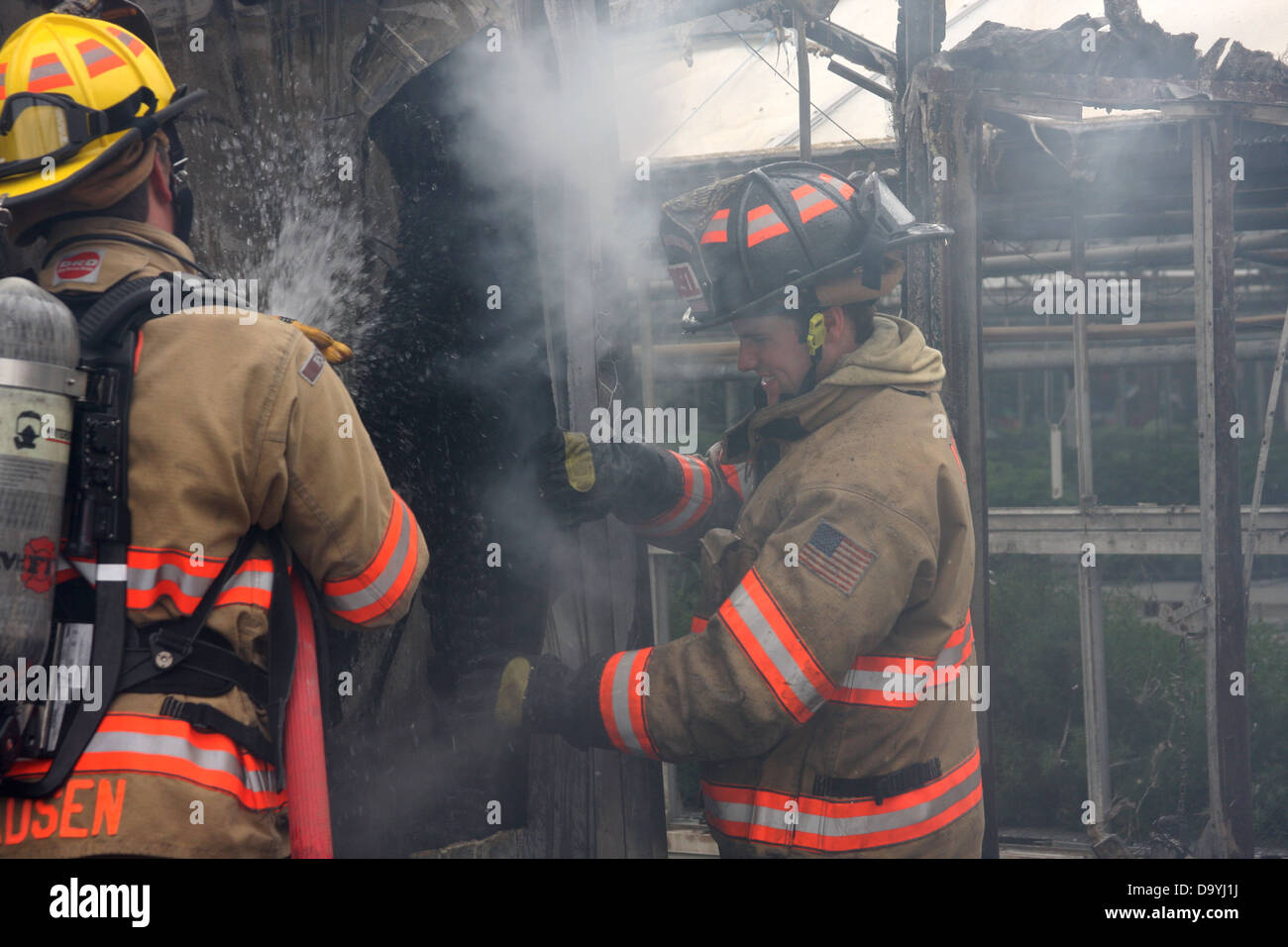 Two firefighters spraying water on a hot spot from a building fire ...