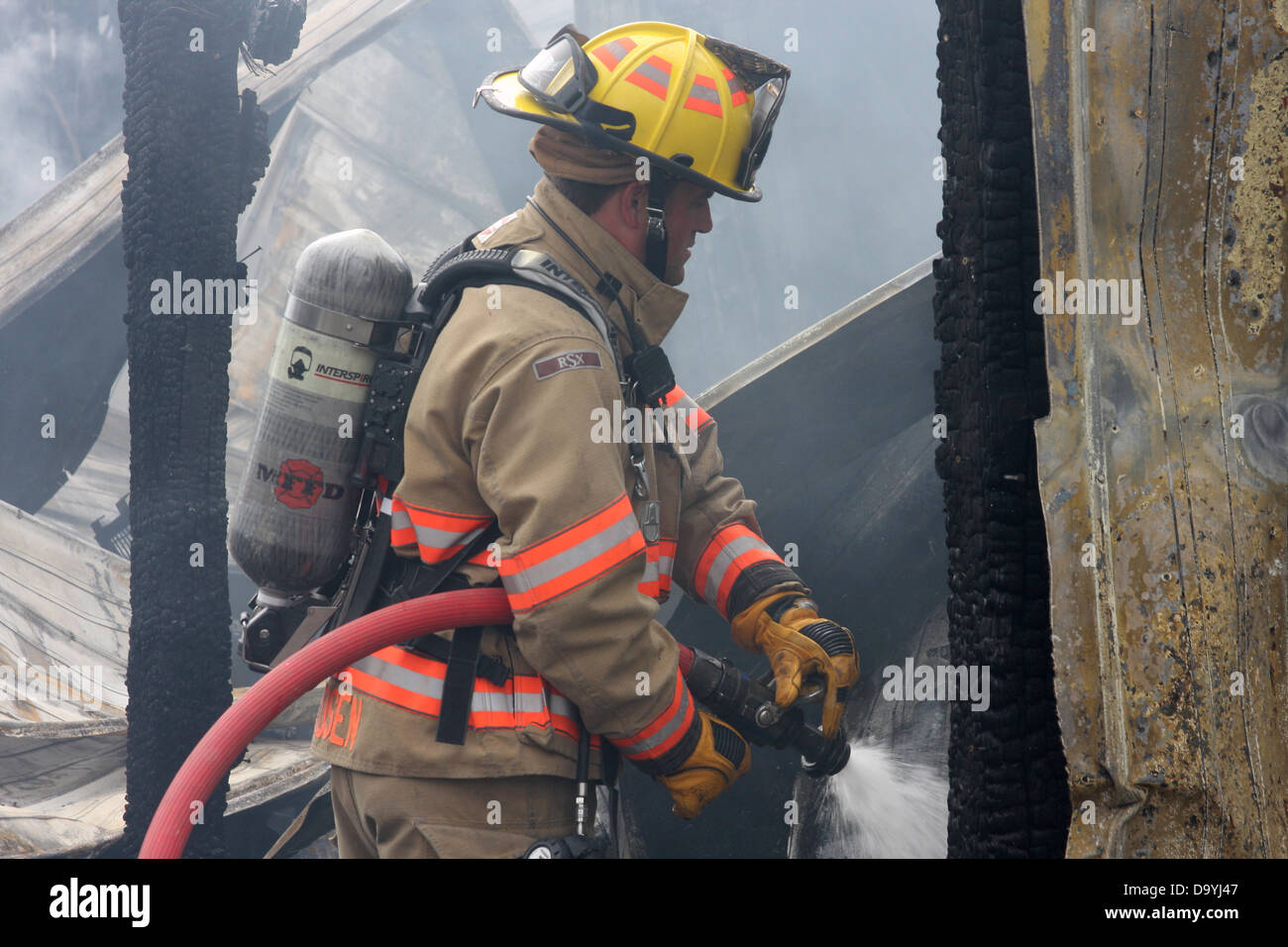 A firefighter spraying water on a structure fire hotspot Stock Photo ...