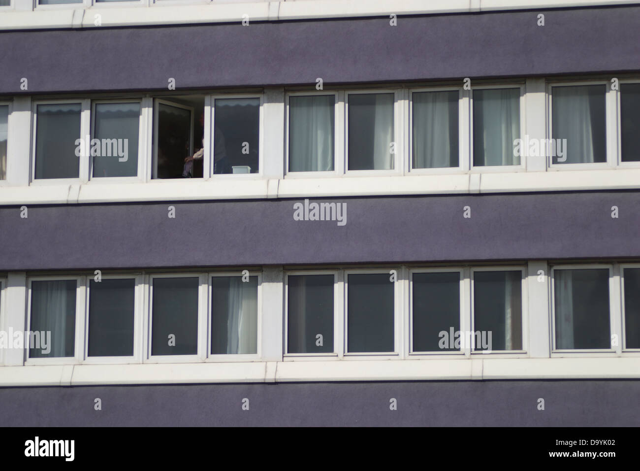 Windows in a block of flats, one is open and being cleaned by a man ...